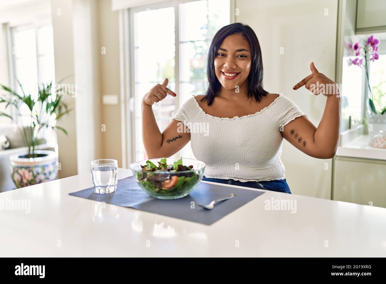 Young hispanic woman eating healthy salad at home looking confident ...