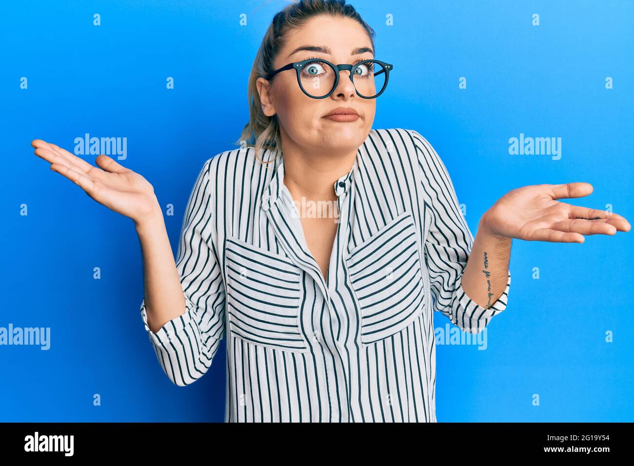 Young caucasian woman wearing business shirt and glasses clueless and ...