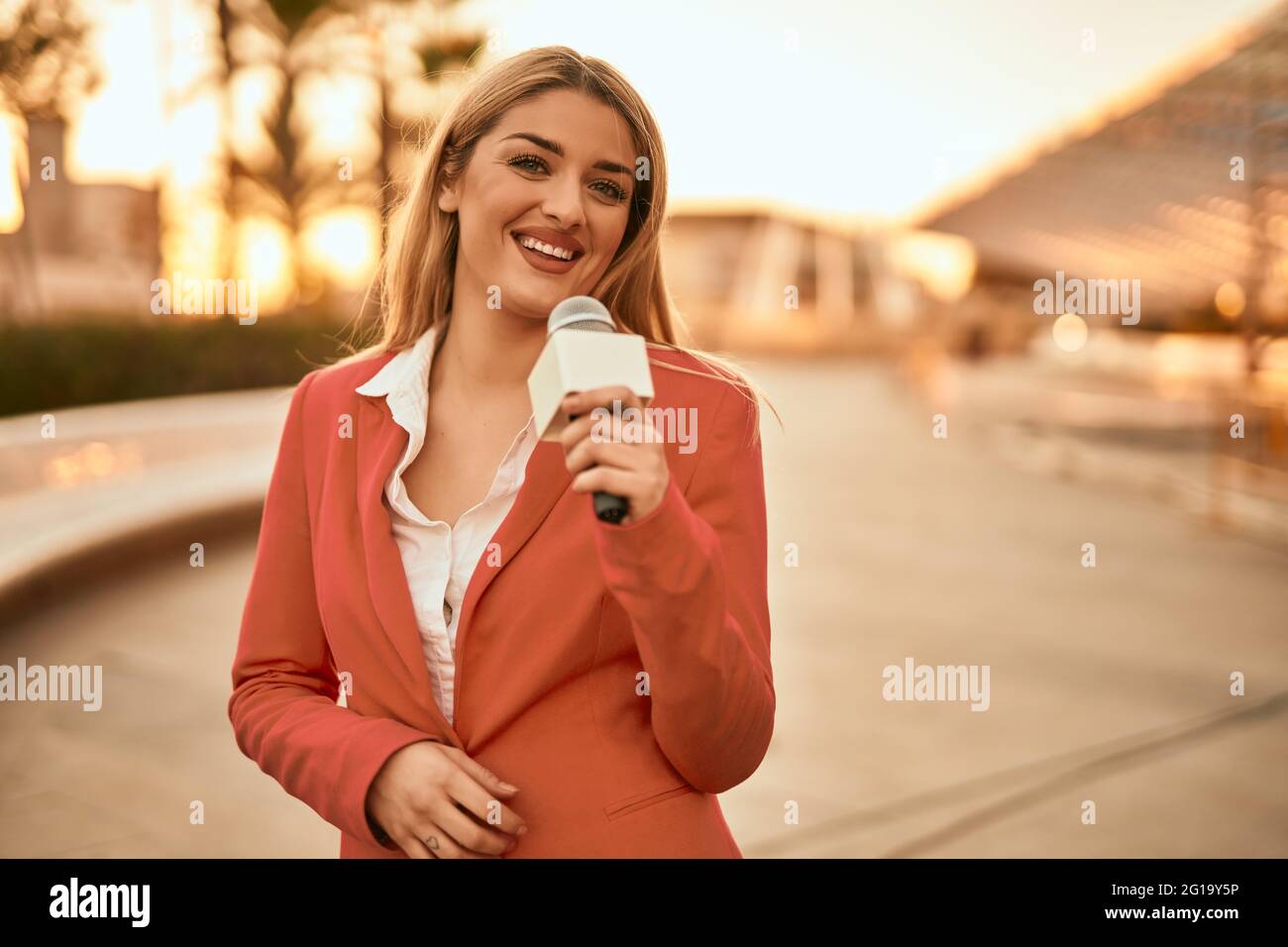 Young blonde reporter woman working using microphone at the city Stock ...