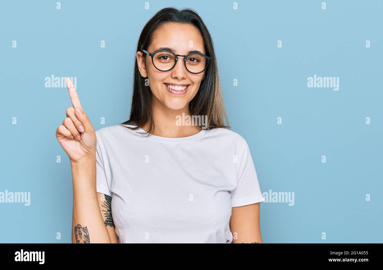 Young hispanic woman wearing casual white t shirt pointing finger up ...