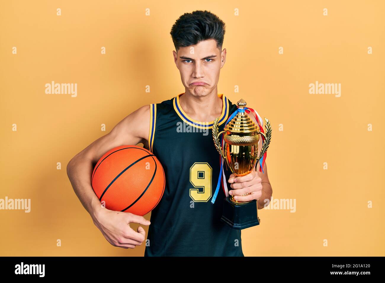 Young hispanic man wearing basketball uniform holding ball and prize ...