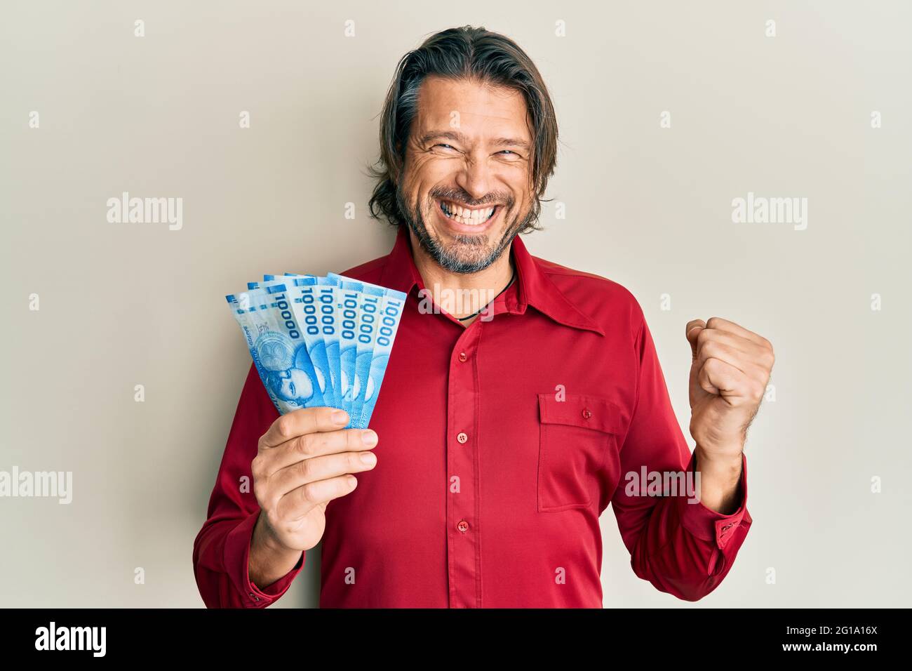 Middle age handsome man holding 10000 chilean pesos screaming proud ...