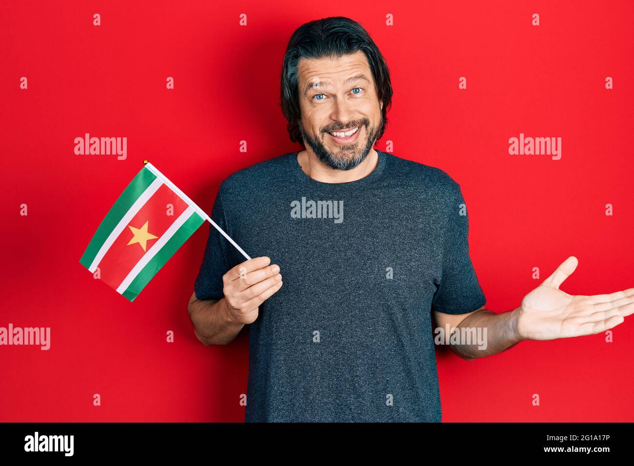Middle age caucasian man holding suriname flag celebrating achievement ...