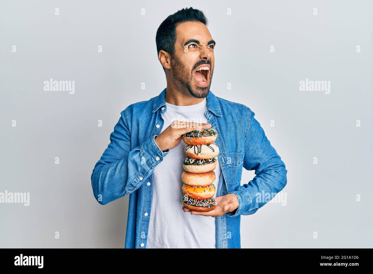 Young hispanic man holding tasty colorful doughnuts angry and mad ...