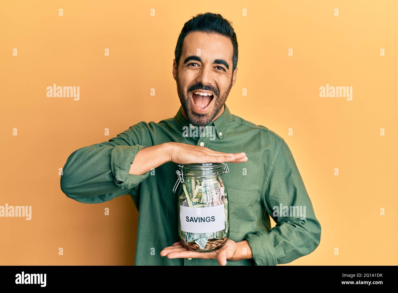 Young hispanic man holding jar with savings smiling and laughing hard ...