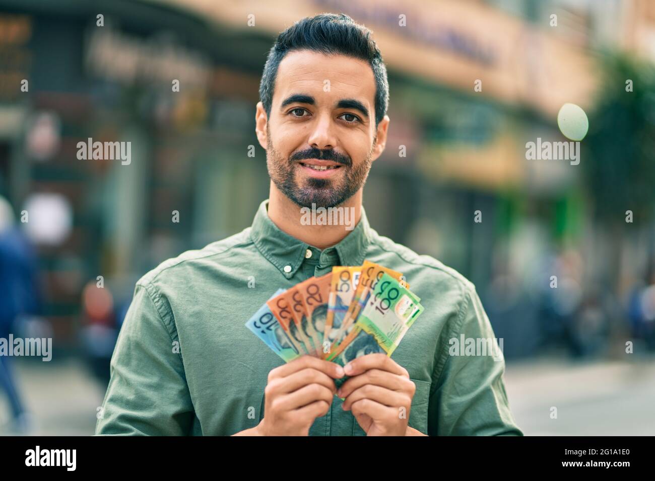 Young hispanic man smiling happy holding australian dollars at the city ...