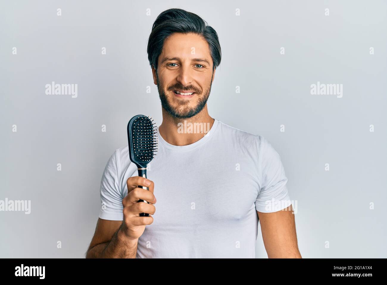 Young hispanic man styling hair using comb looking positive and happy ...