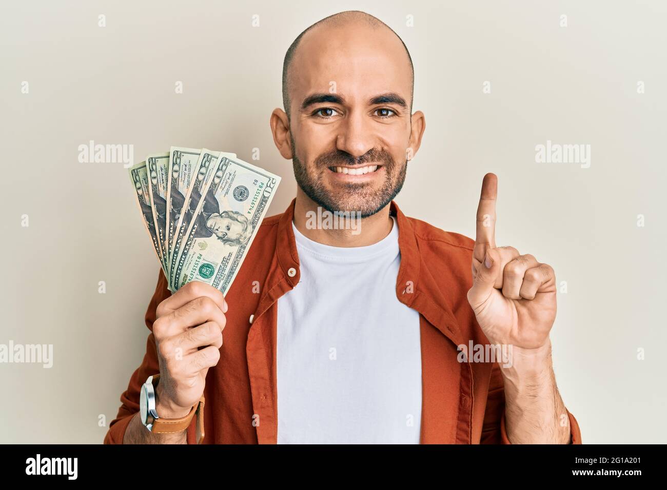 Young hispanic man holding 20 dollars banknote smiling with an idea or ...