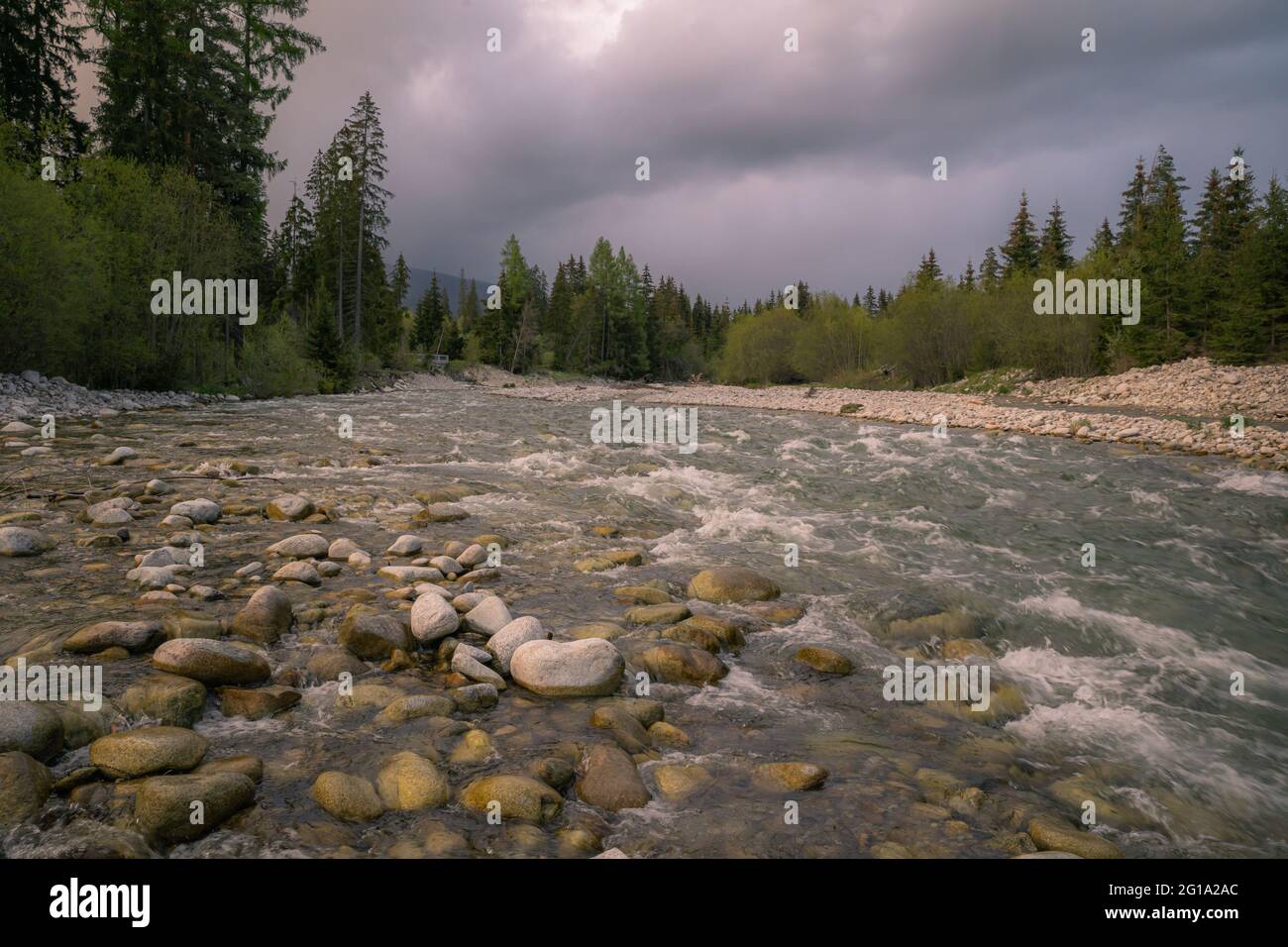 A stormy mountain river flows in a valley with rocks on the banks and a cloudy sky above it ...