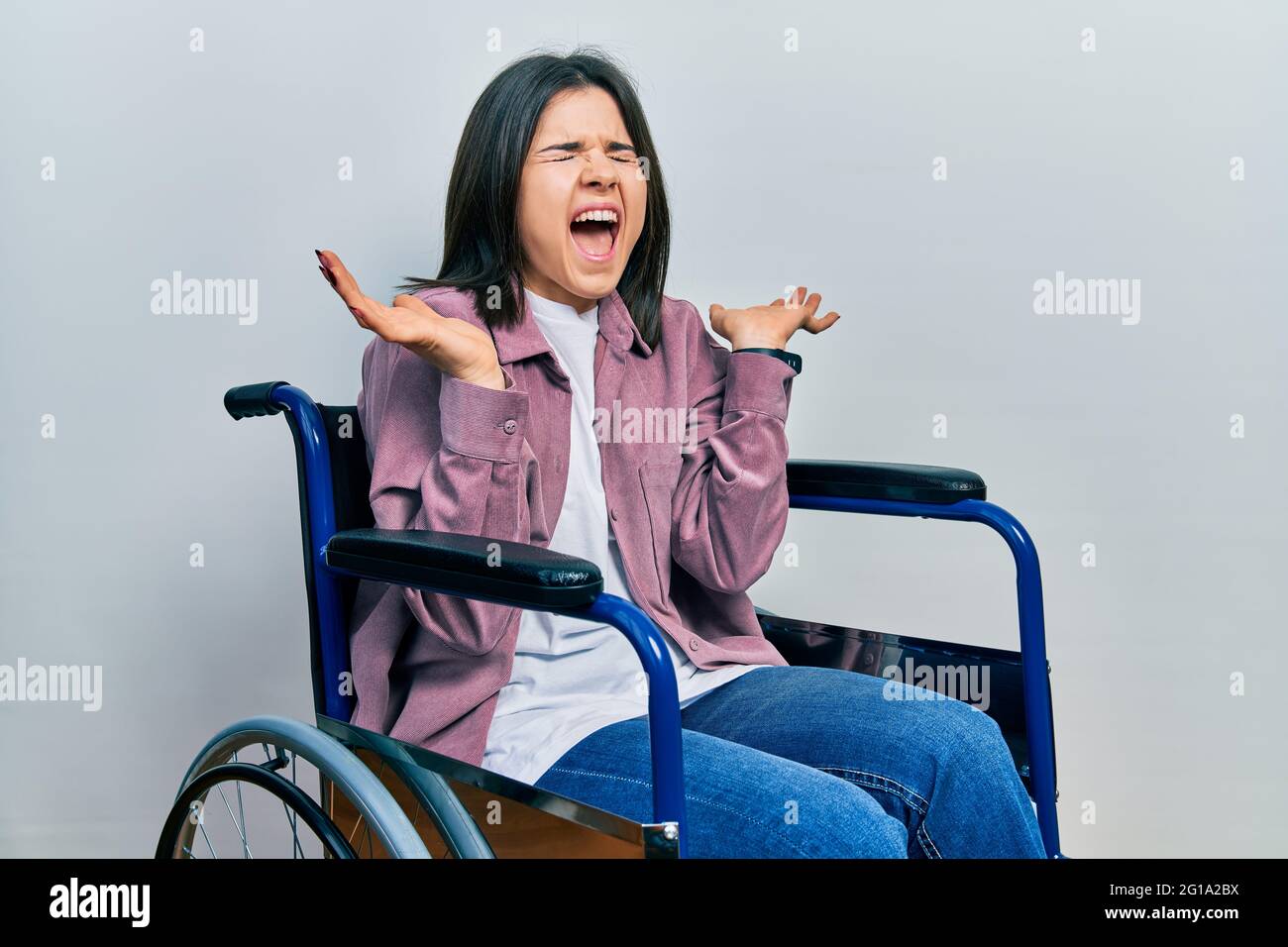 Young brunette woman sitting on wheelchair celebrating mad and crazy ...
