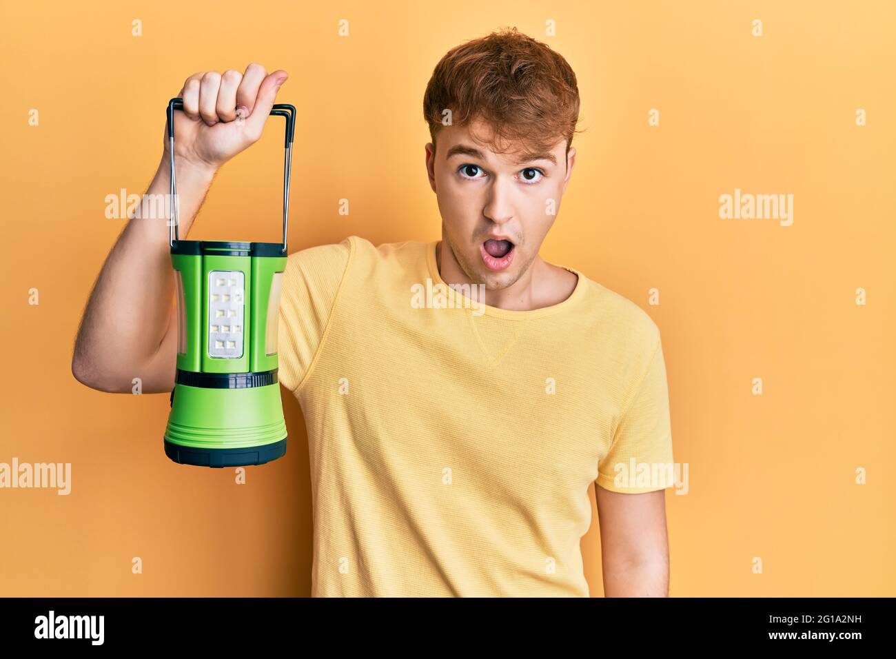 Young caucasian man holding big electric lantern scared and amazed with ...