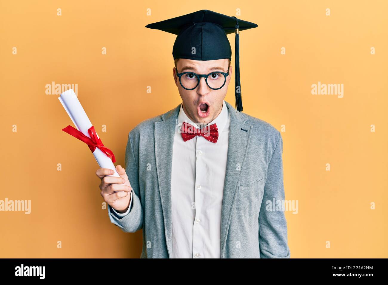 Young caucasian nerd man wearing glasses and graduation cap and holding ...