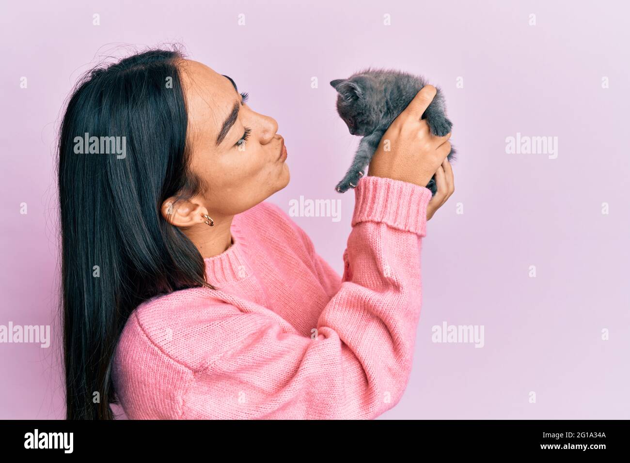 Young hispanic girl smiling happy holding cute cat over isolated pink ...