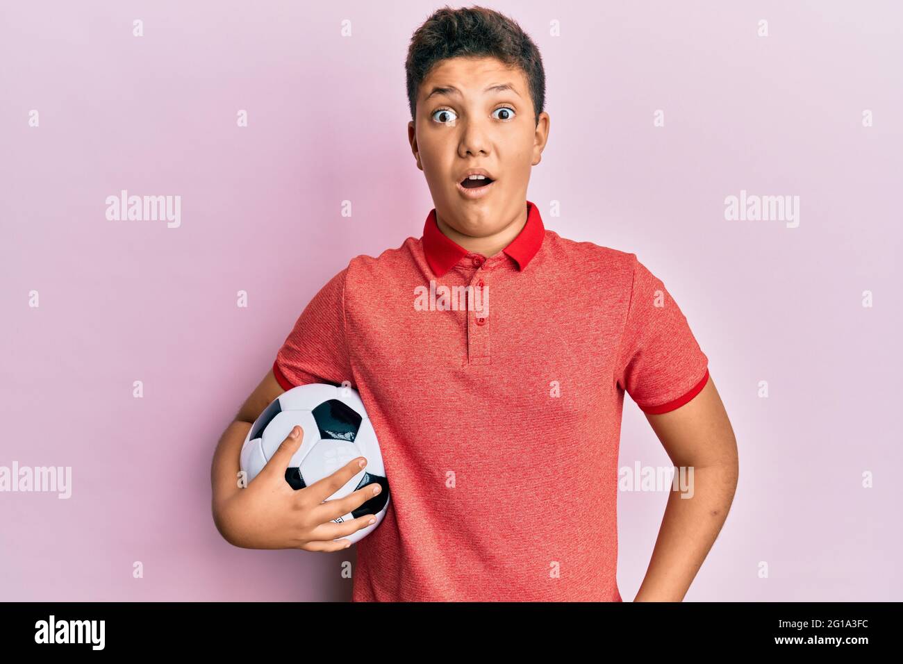Teenager hispanic boy holding soccer ball scared and amazed with open ...