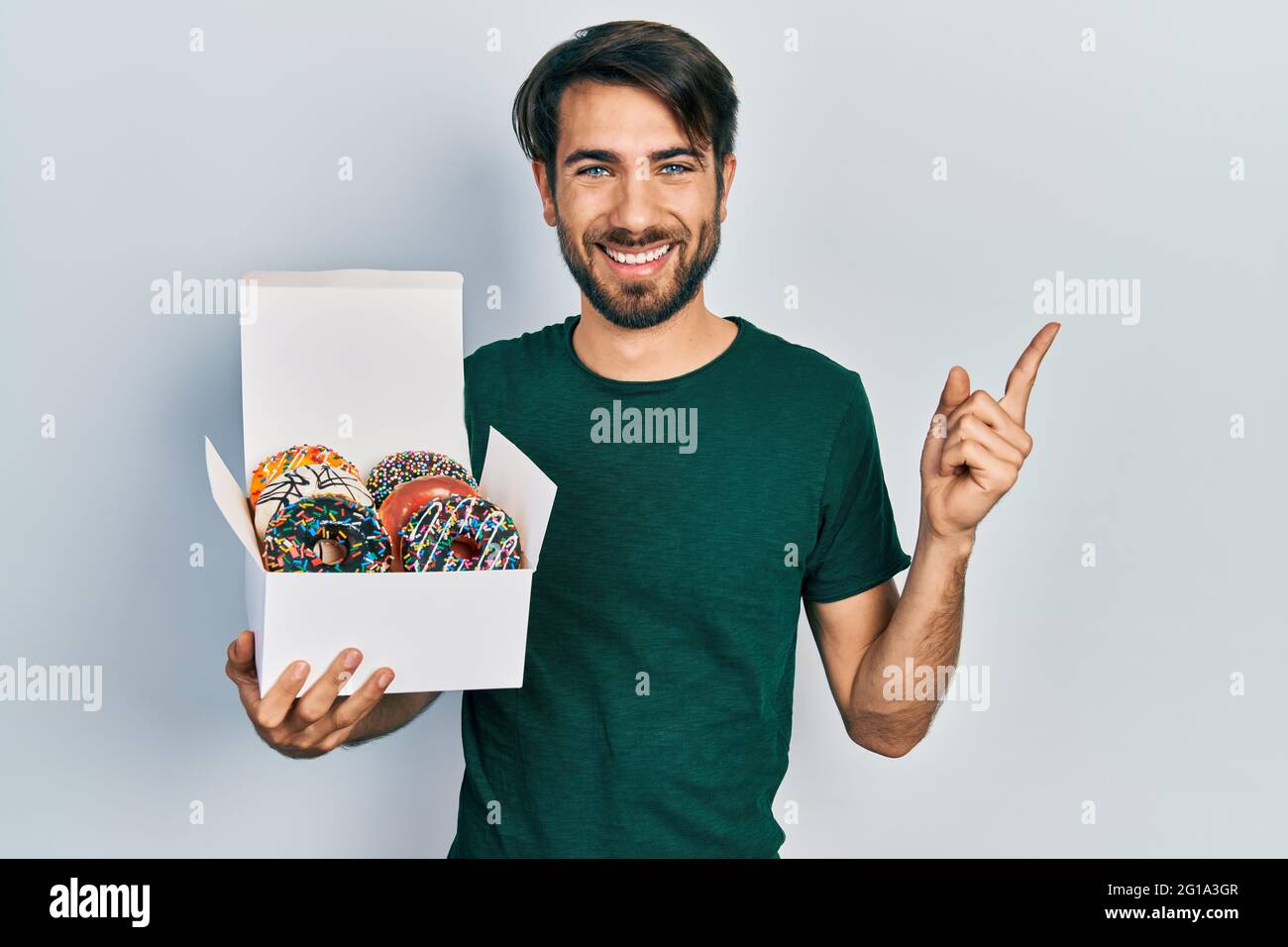Young hispanic man holding box of tasty colorful doughnuts smiling ...