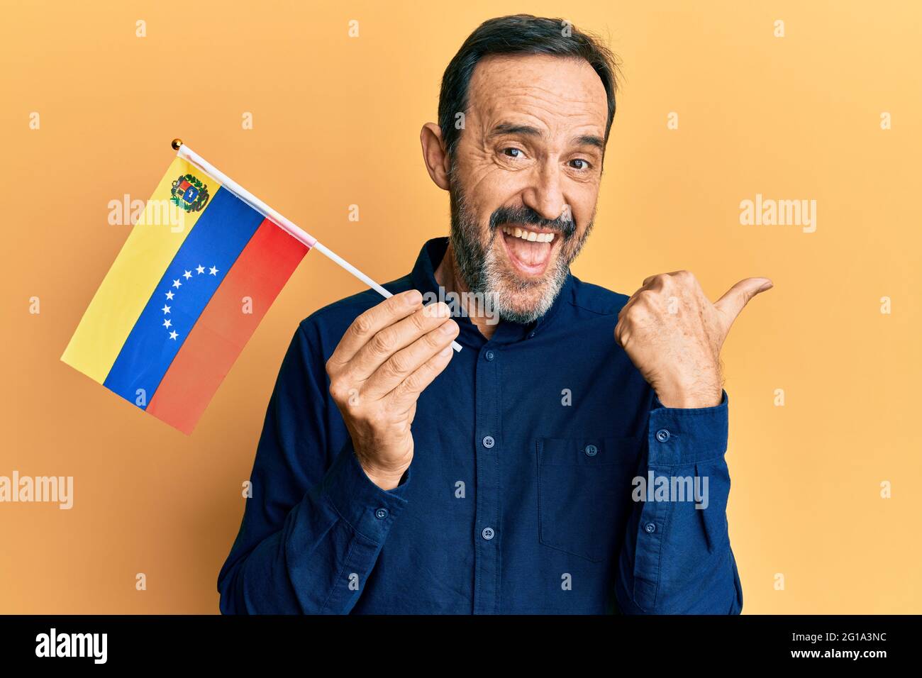 Middle age hispanic man holding venezuelan flag pointing thumb up to ...