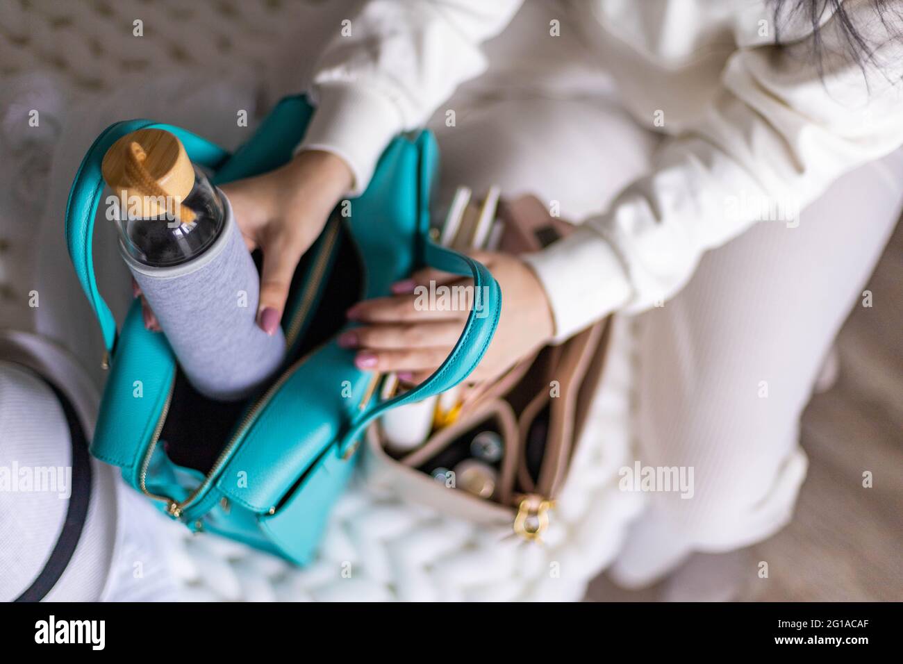 Closeup female hands putting reusable water bottle into handbag getting ...