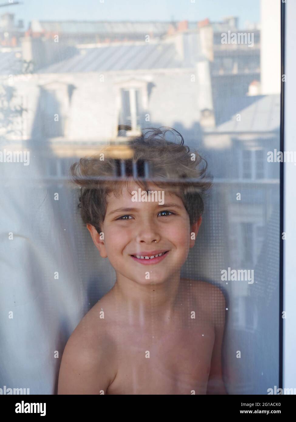 A cute little boy stands in the room by the window. Reflection in the ...