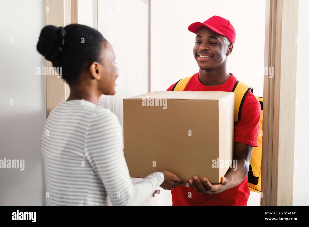 African American Courier Giving Box To Female Standing In Doorway Stock ...