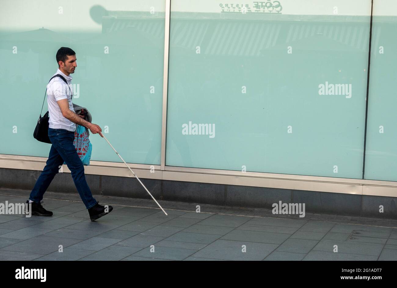 Young sightless man walking quickly with a cane in the city centre of ...