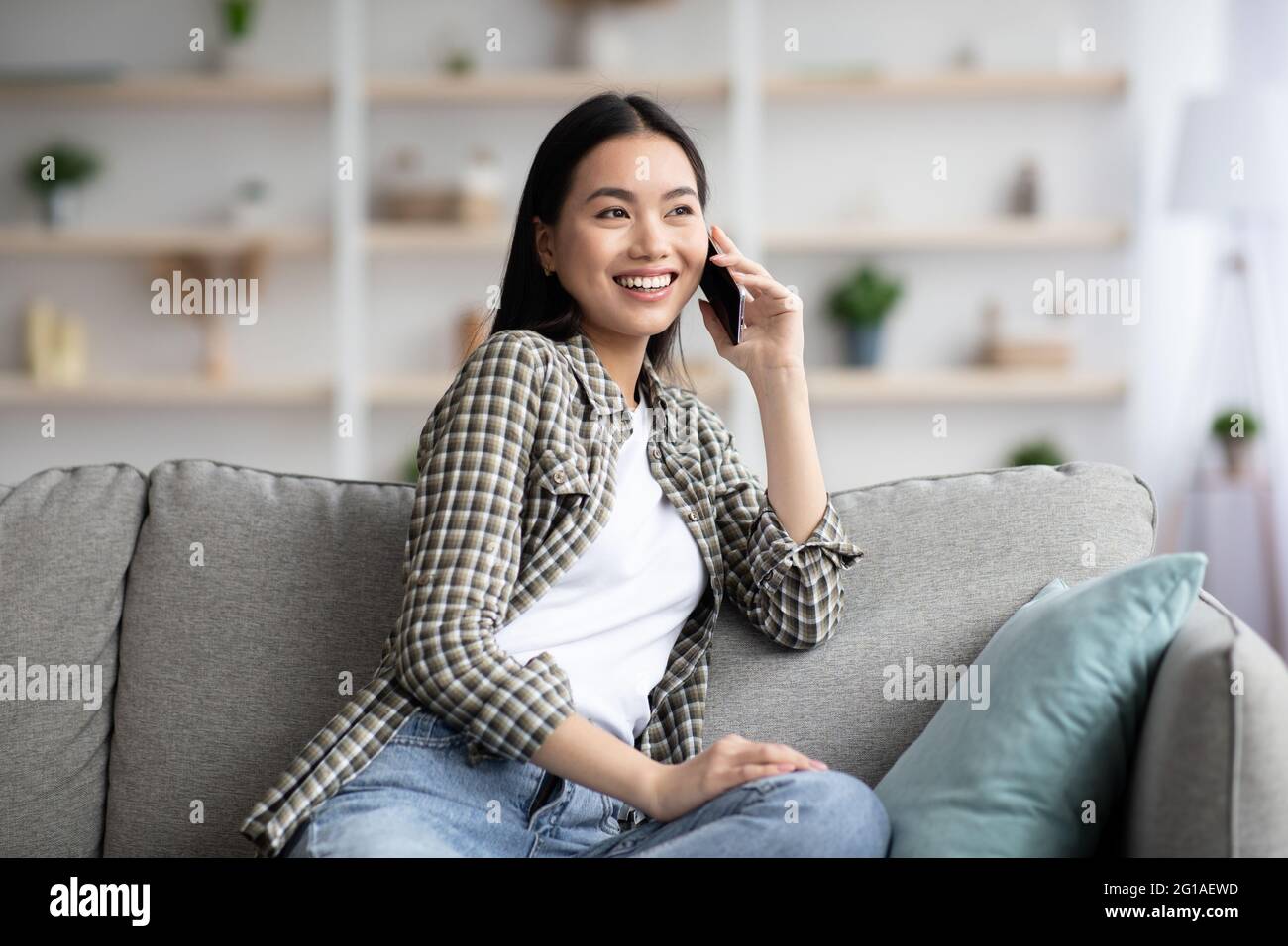 Cheerful asian lady sitting on sofa and talking on smartphone Stock ...