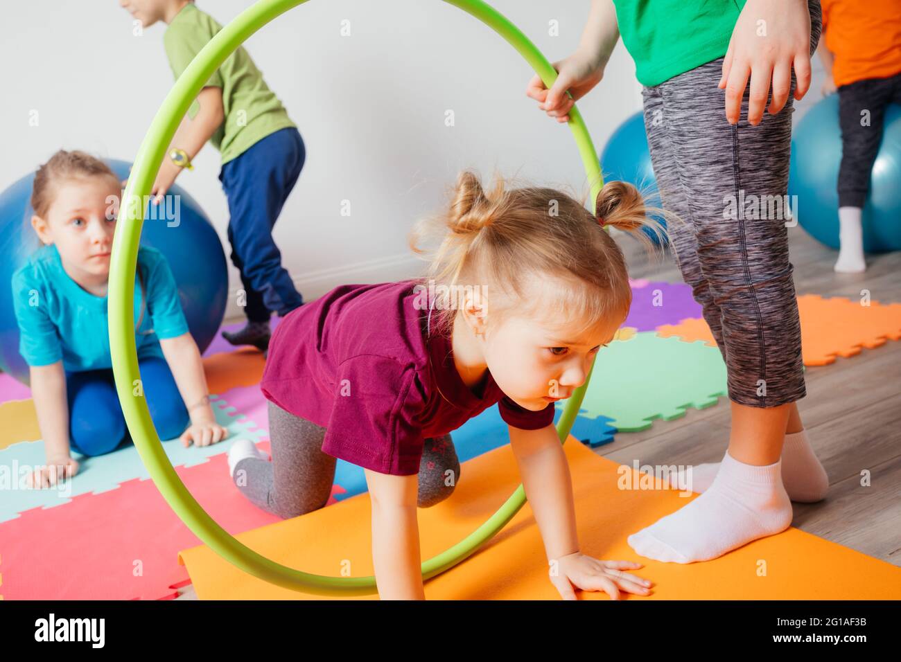Curly girl crawling on colorful floor through hula hoops Stock Photo ...