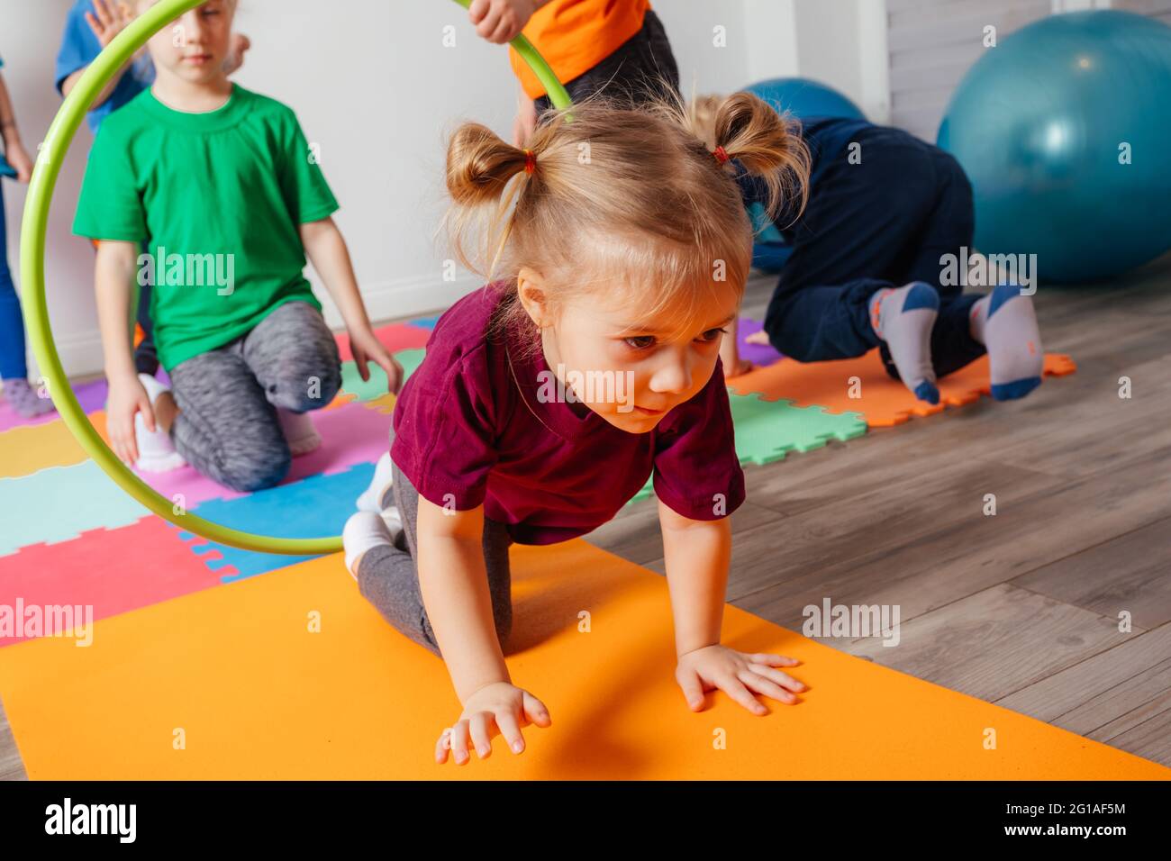 Curly girl crawling on colorful floor through hula hoops Stock Photo ...