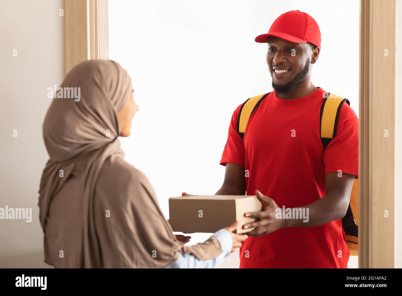 Black delivery man holding box giving it to muslim customer Stock Photo ...