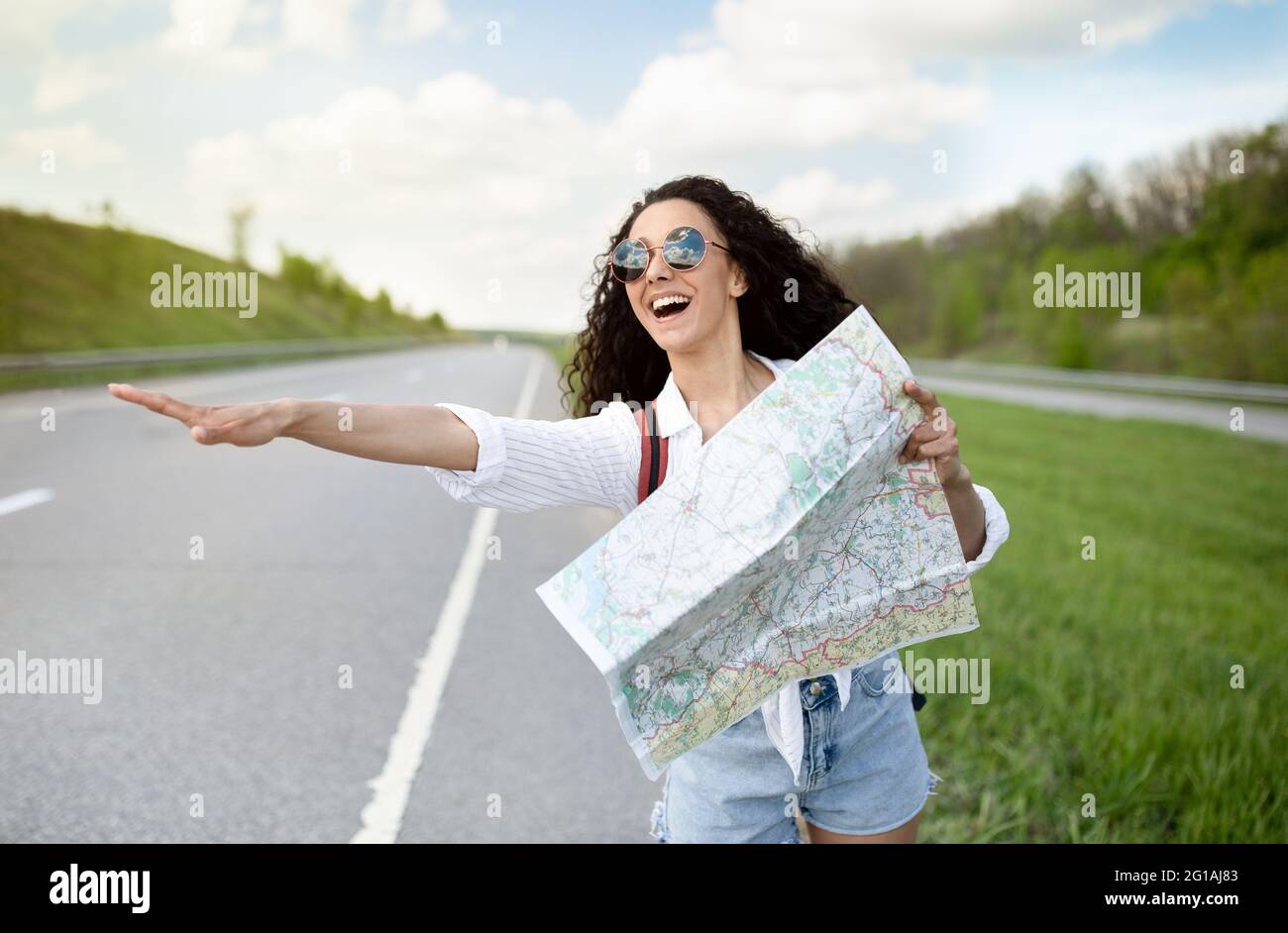 Young female tourist with map catching ride, stopping vehicle ...