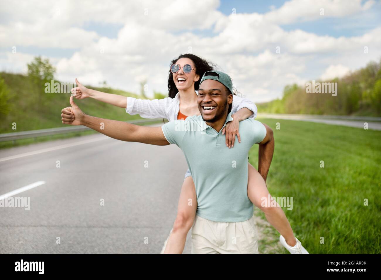 African American guy giving his girlfriend piggyback ride on highway ...