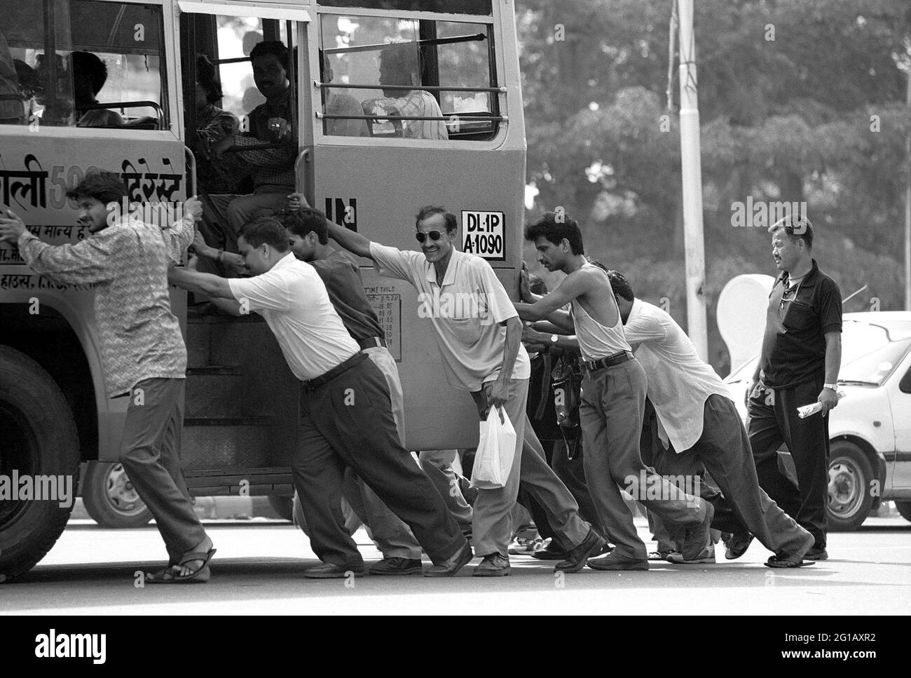 India, New Delhi. Passengers help push start a bus in New Delhi. July ...