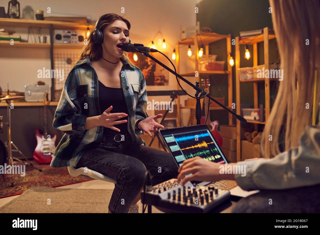 Blond girl singing in microphone while her friend recording new songs ...