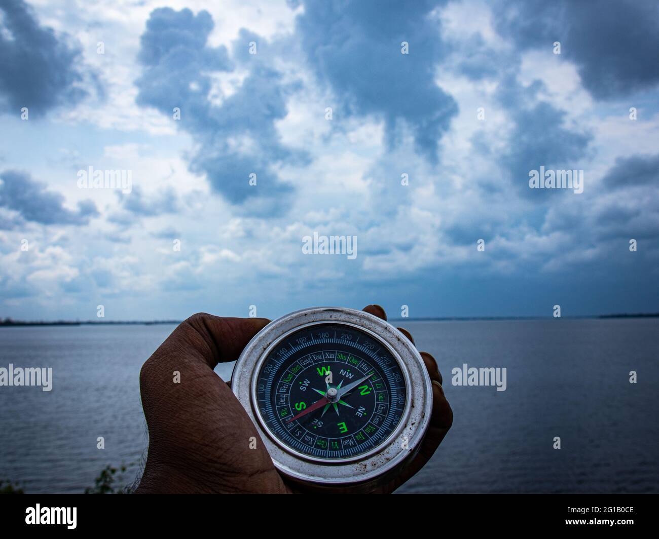 A hand holding a compass near a sea under the beautiful sky Stock Photo ...