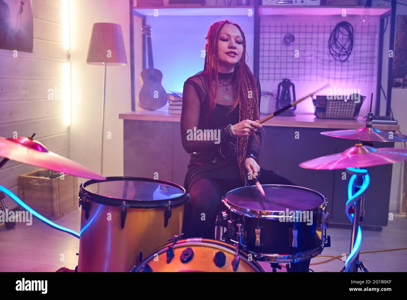 Young female with braids hitting cymbals of drum kit during repetition ...