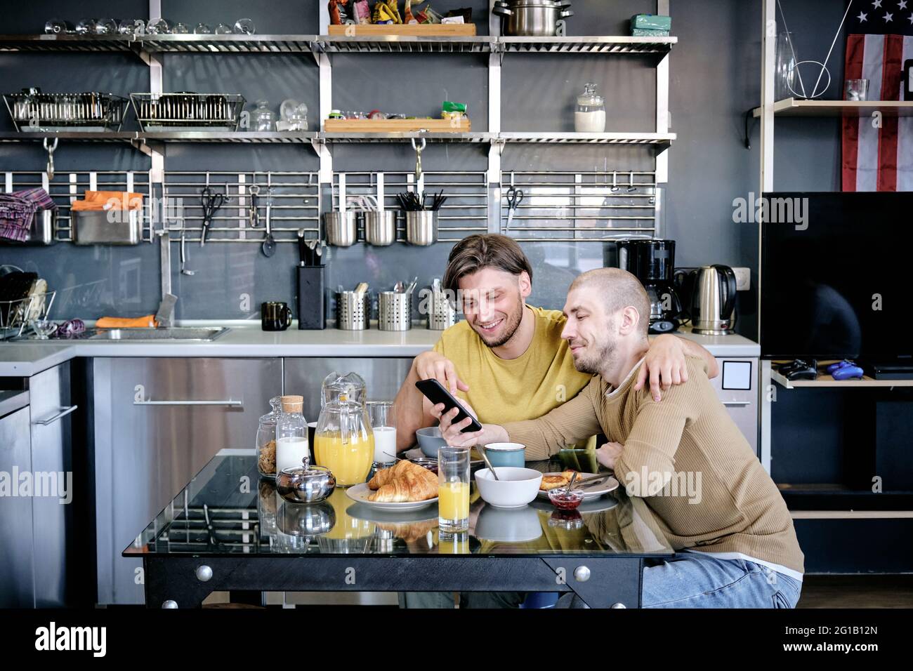 Two men scrolling in smartphone over kitchen table during breakfast ...