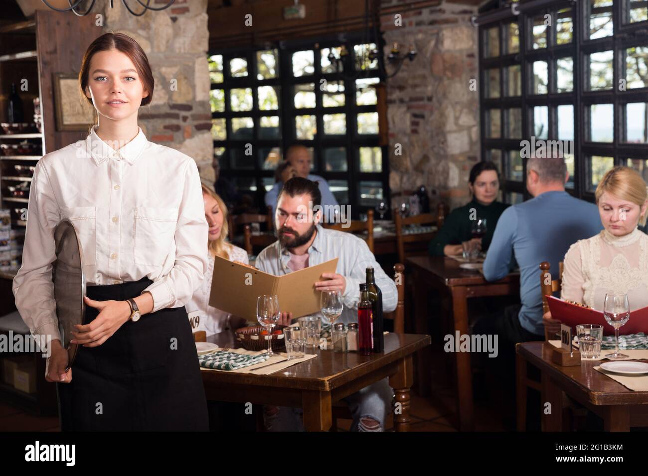 Positive woman waiter demonstrating country restaurant to visitors ...