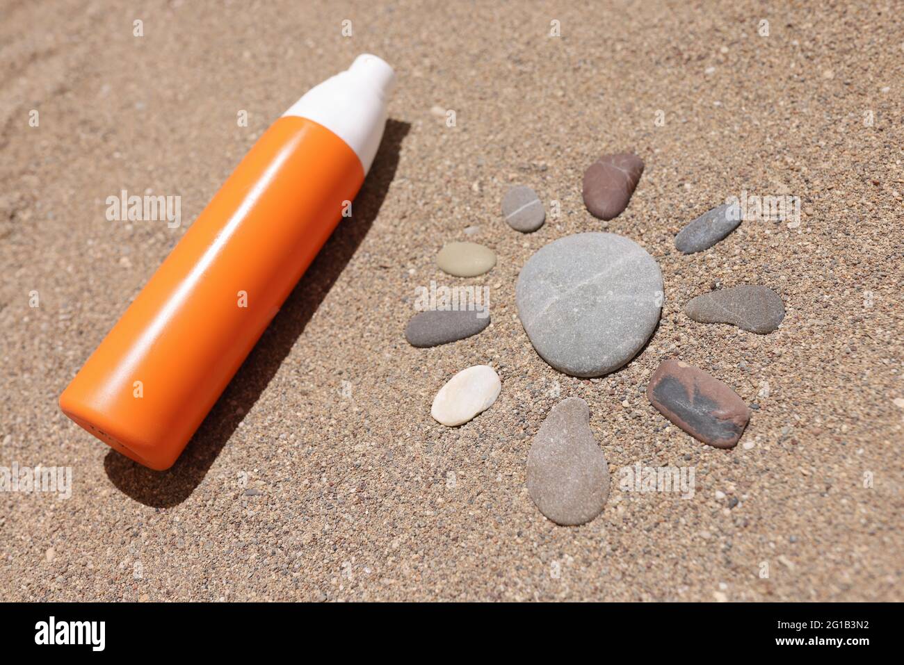 Sunscreen lotion lies on hot sand next to sun figure made of stones ...