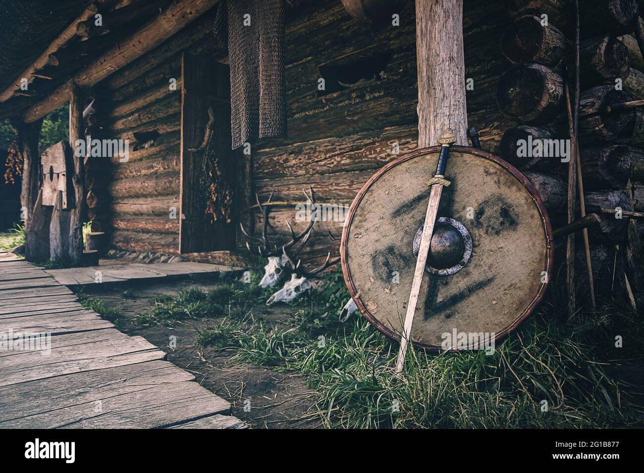 Ancient sword and shield weapons lie in front of an old medieval hut ...