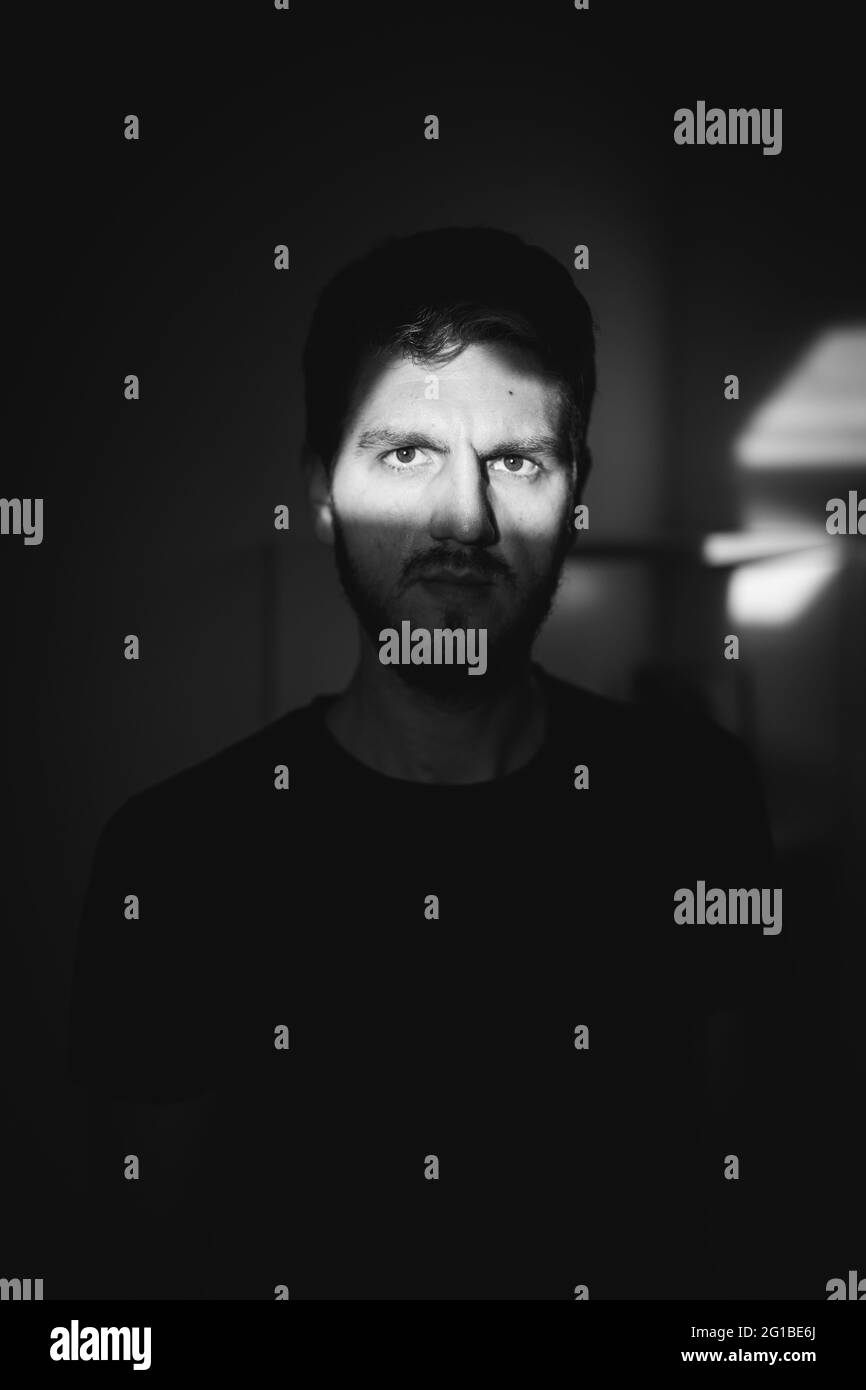 A grayscale shot of a handsome guy looking at the window with sun rays ...