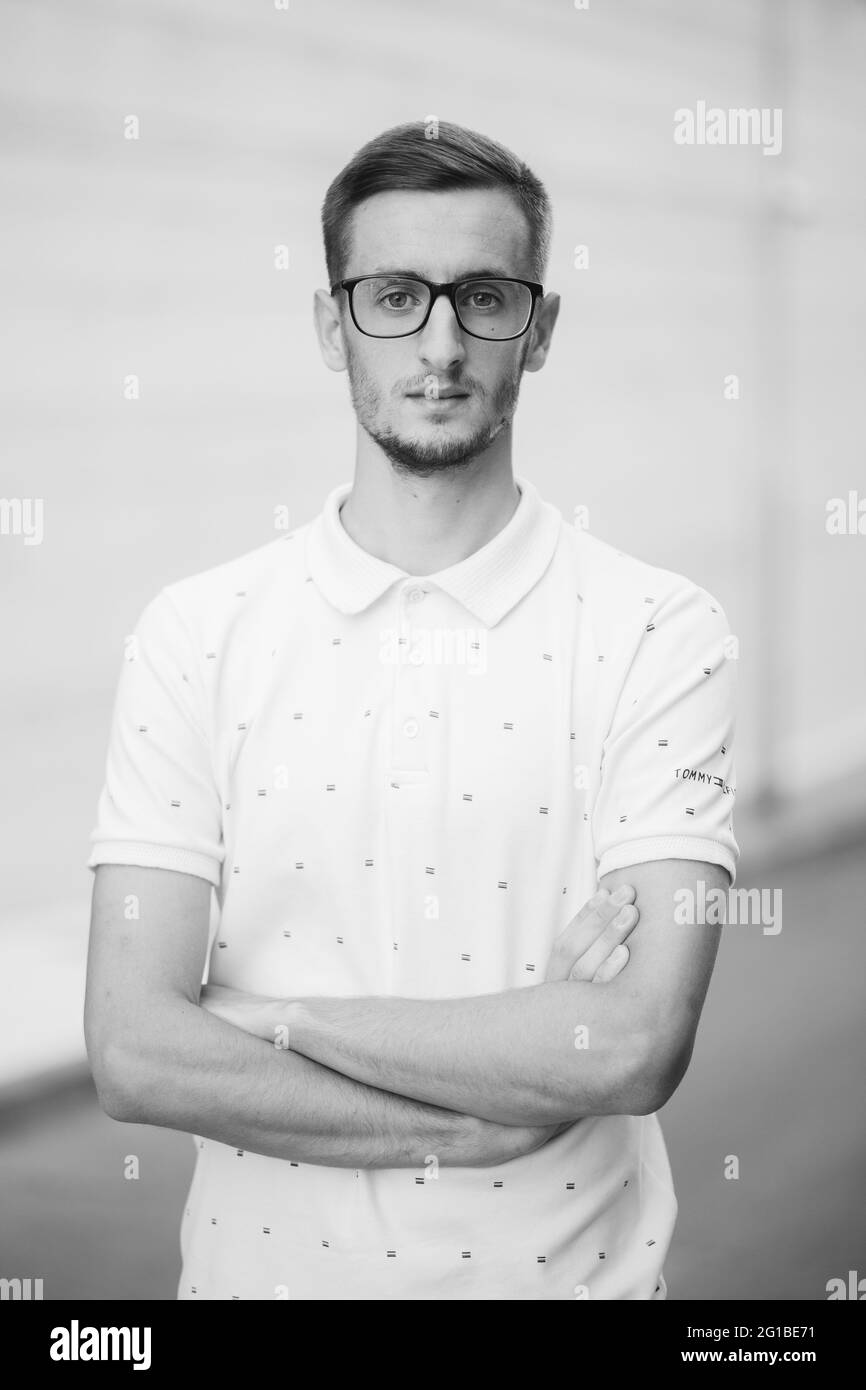 A grayscale shot of a handsome guy in glasses with his hands crossed ...