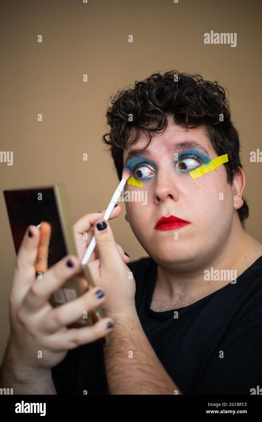 Concentrated eccentric feminine male applying eyes color with brush ...