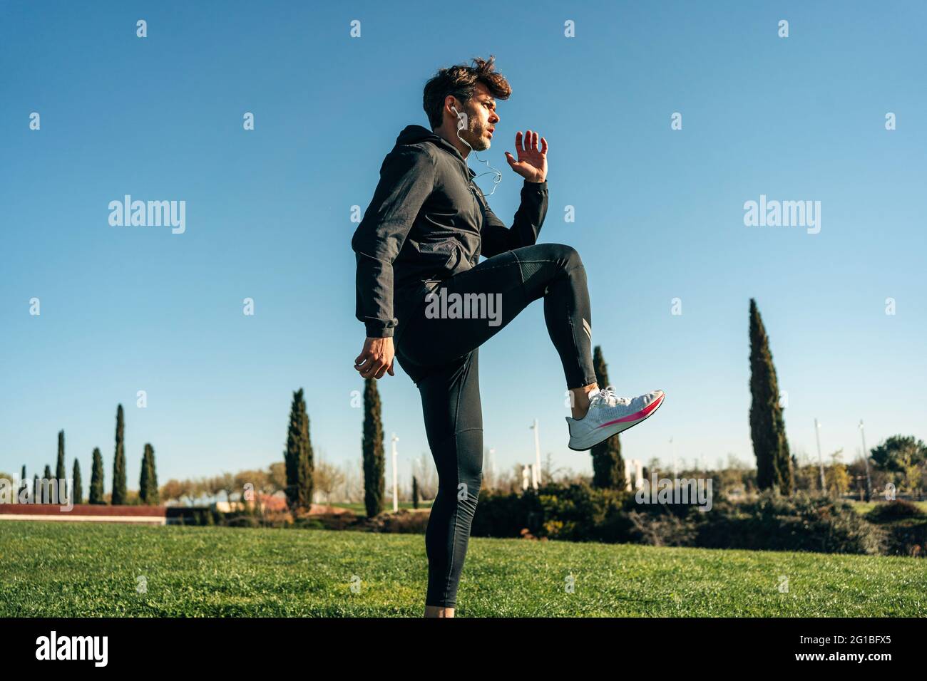 Adult male athlete in sports clothes raising leg and looking forward ...