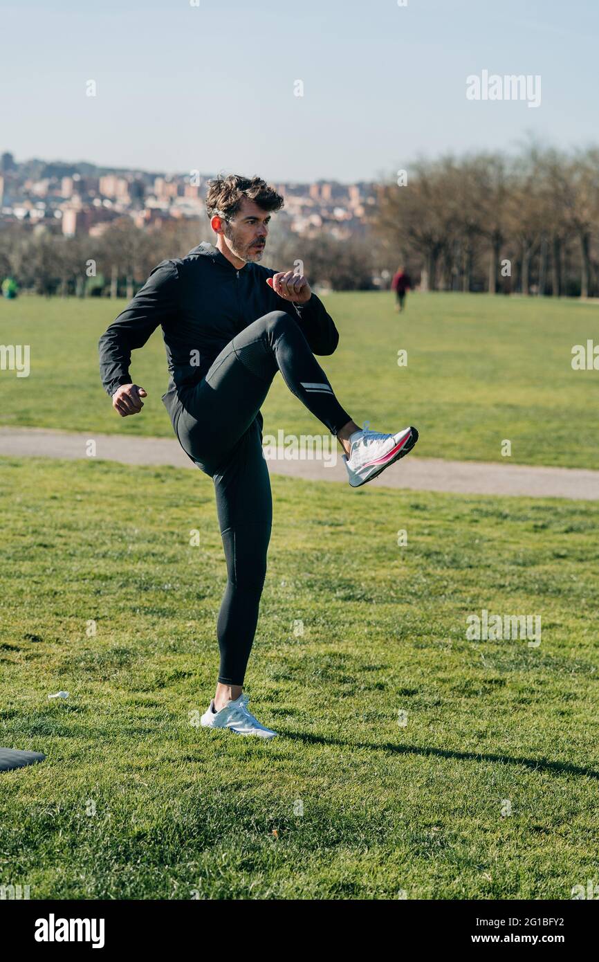 Adult male athlete in sports clothes raising leg and looking forward ...