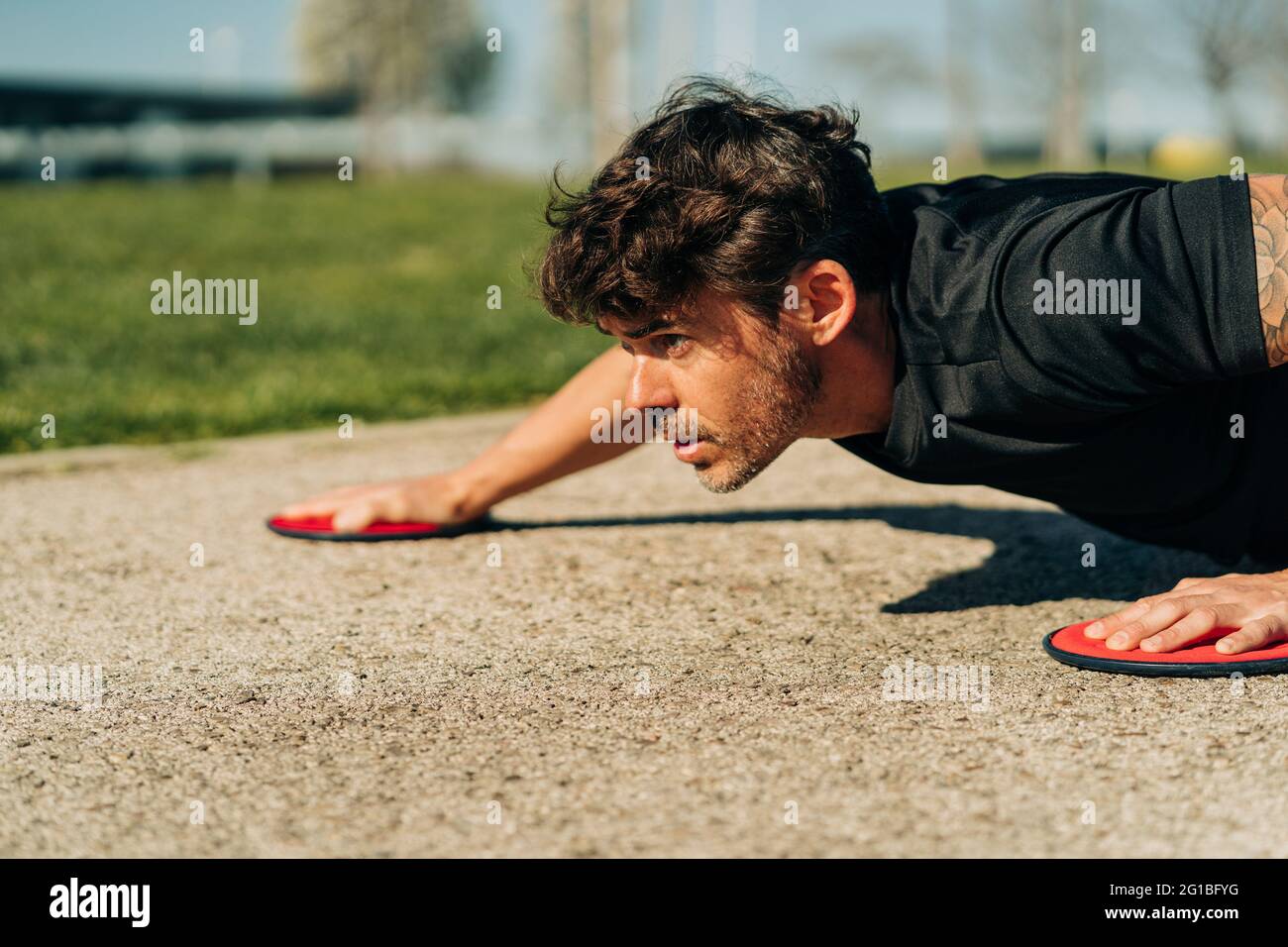 Ground level of attentive male athlete in plank pose with gliding discs ...