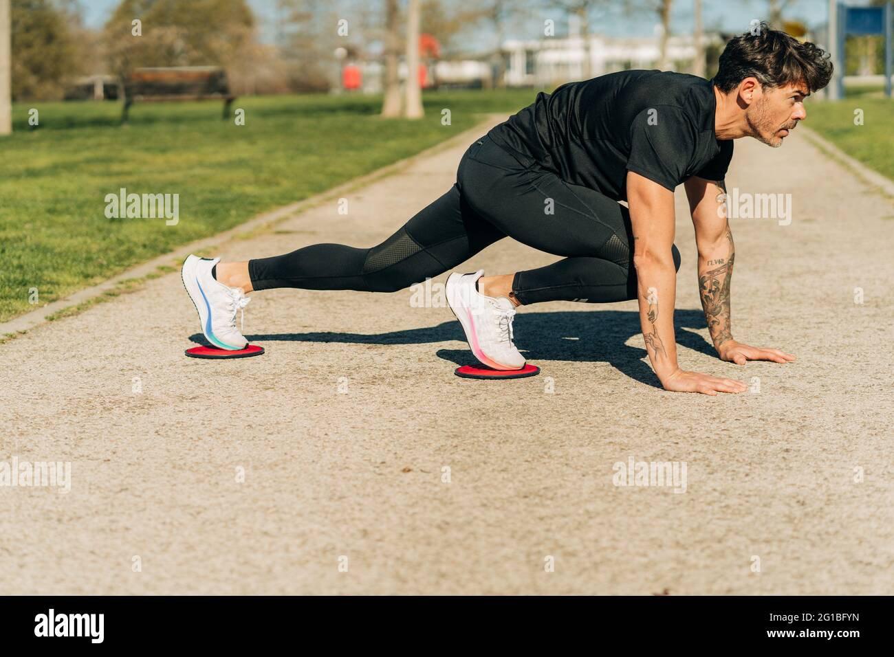 Ground level of attentive male athlete in plank pose with gliding discs ...