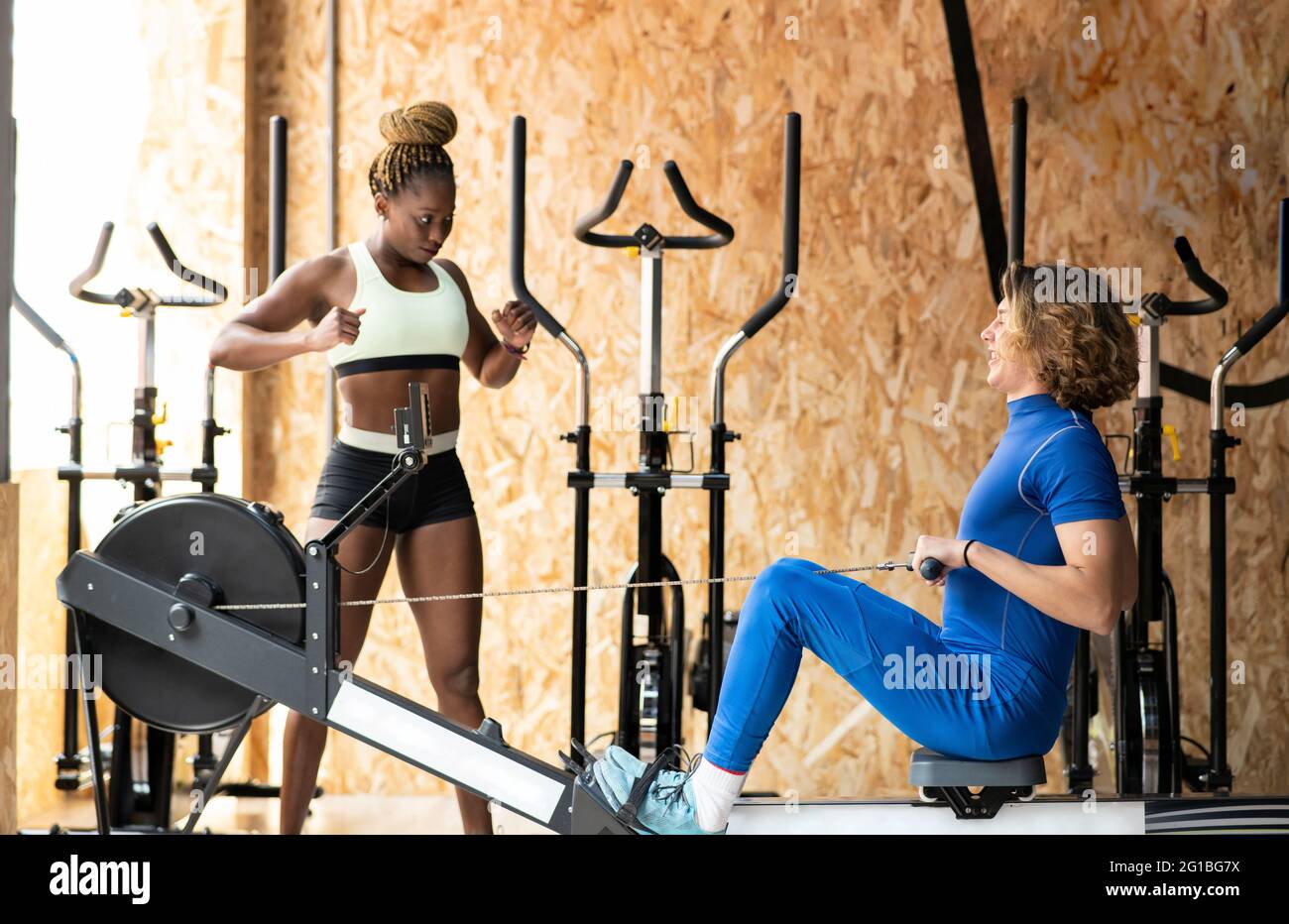 Smiling male athlete working out on rowing equipment and speaking with ...