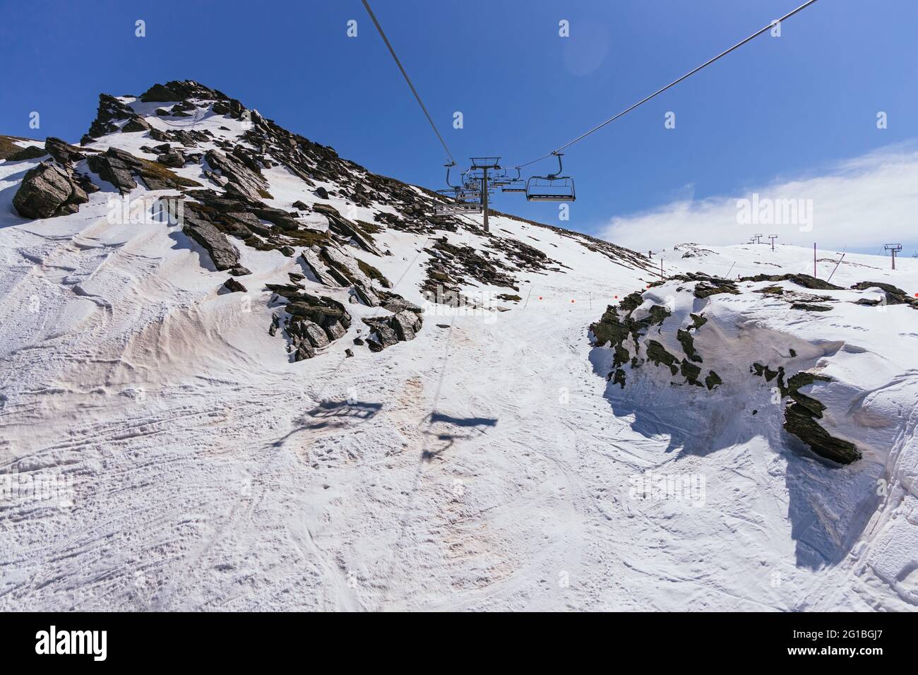 Ropeway with cabins over rough ridge with snow under cloudy blue sky in ...