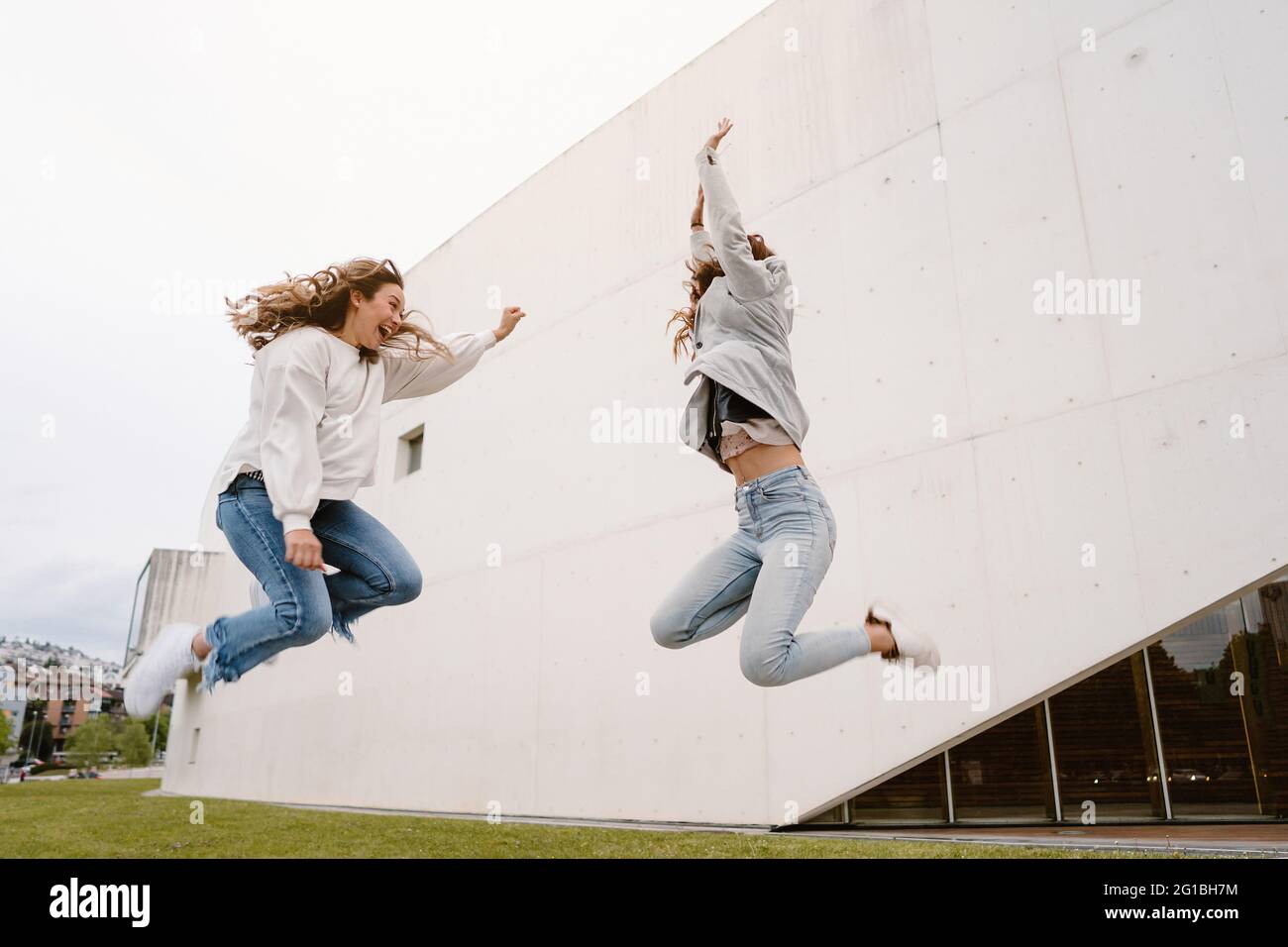 Low angle full body joyful young female best friends jumping together ...