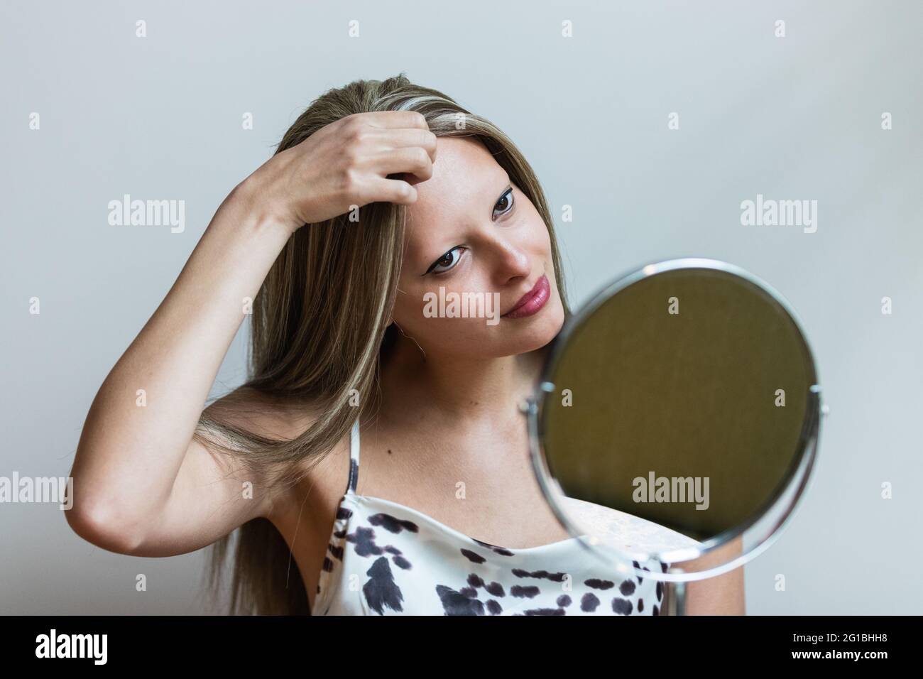 Young confident lady with alopecia looking in mirror and taking off wig ...