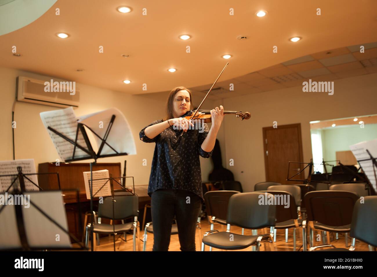 Focused professional female musician playing acoustic violin with eyes ...
